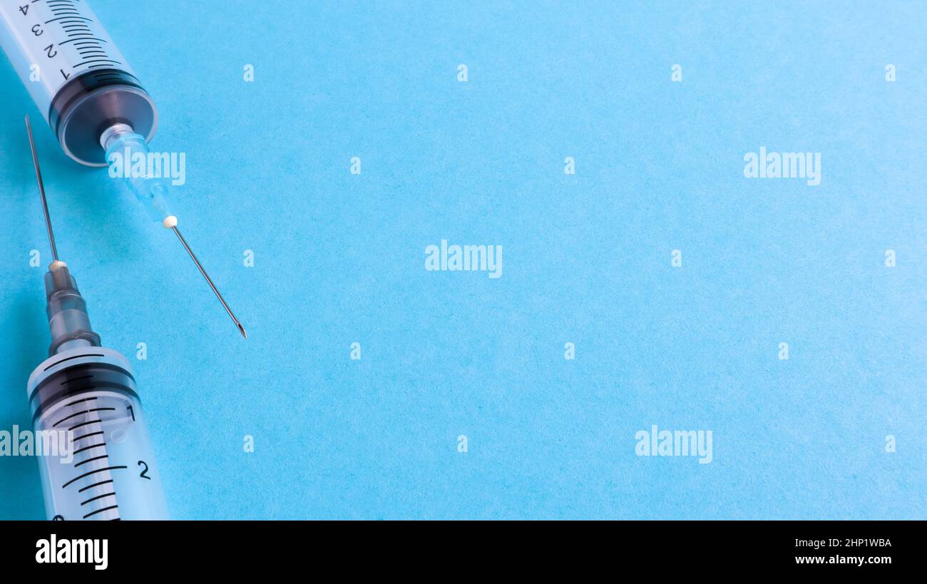 Two empty disposable plastic syringes with needles on a blue background ...