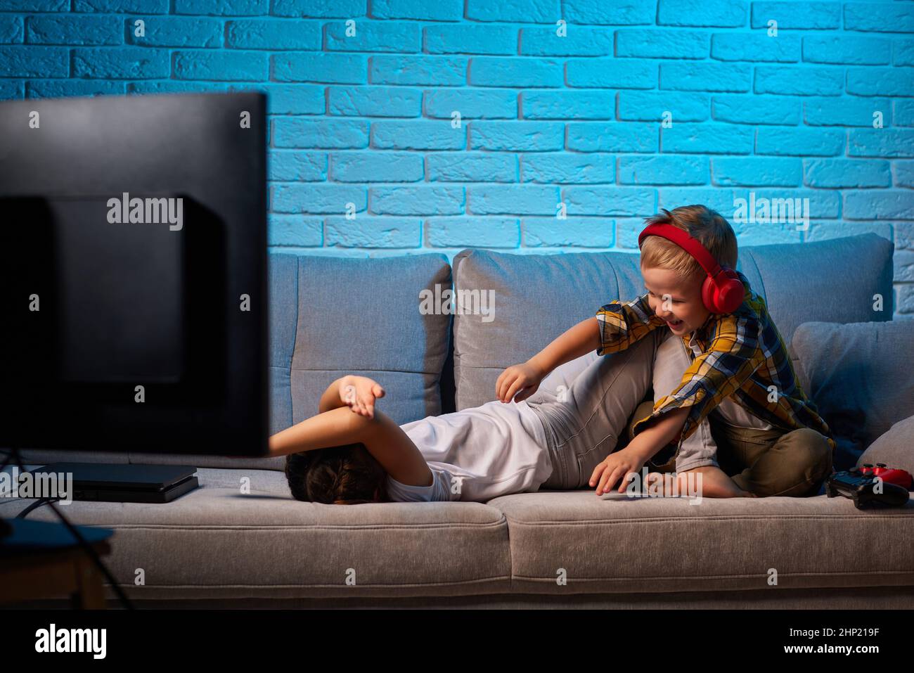 cheerful boy and girl tickle fun while sitting together on the couch ...