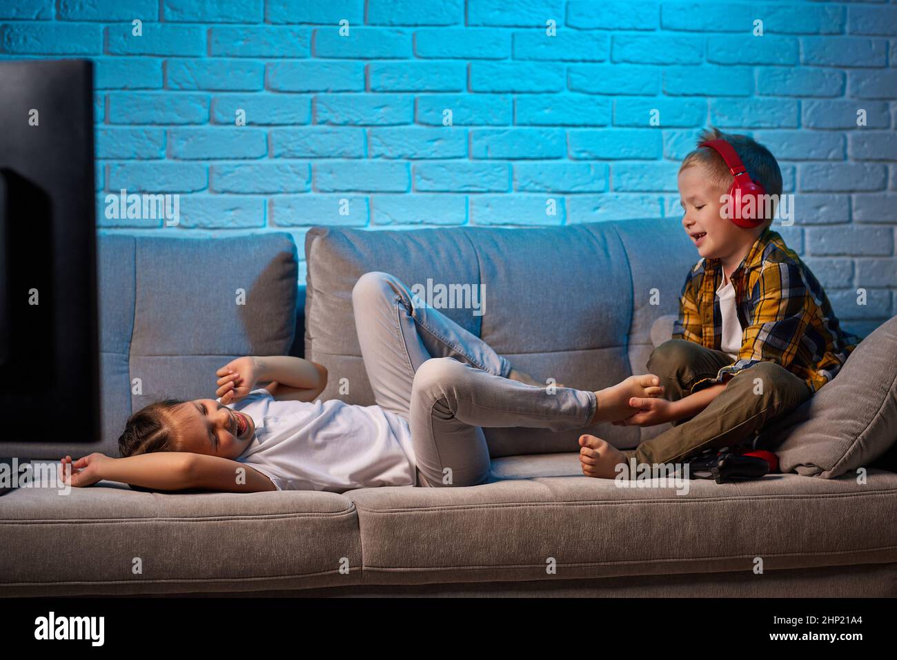 cheerful boy and girl tickle fun while sitting together on the couch ...