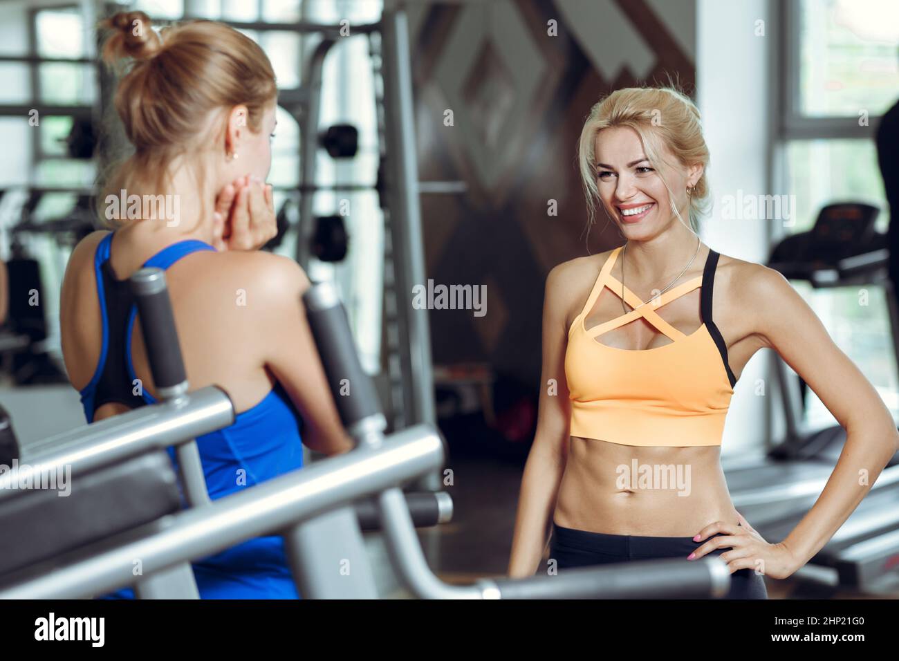 Two athletic blond women talking in the gym. Girl communicates with the ...