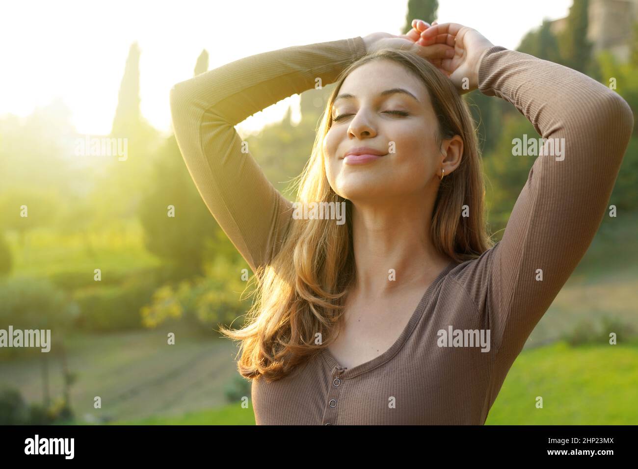 Portrait of free woman breathing clean air in nature. Happy girl with raised arms in bliss ...