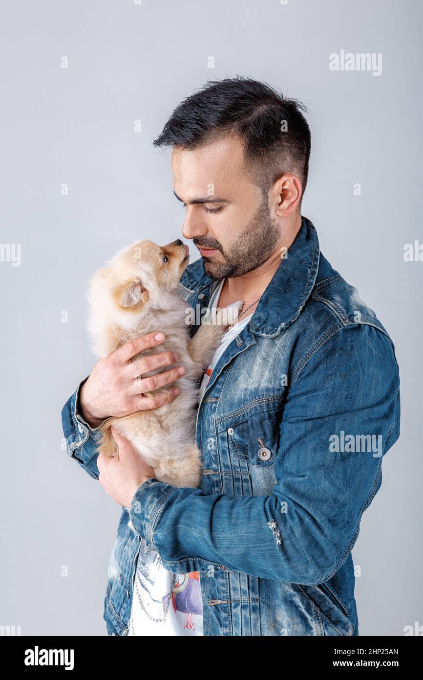 handsome smiling man in denim jacket holds pomeranian dog. Spitz ...