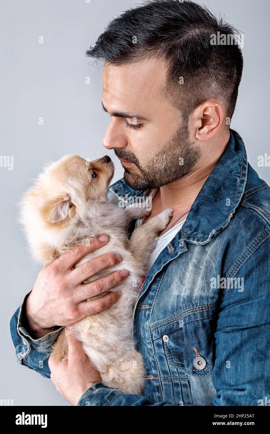 handsome smiling man in denim jacket holds pomeranian dog. Spitz ...