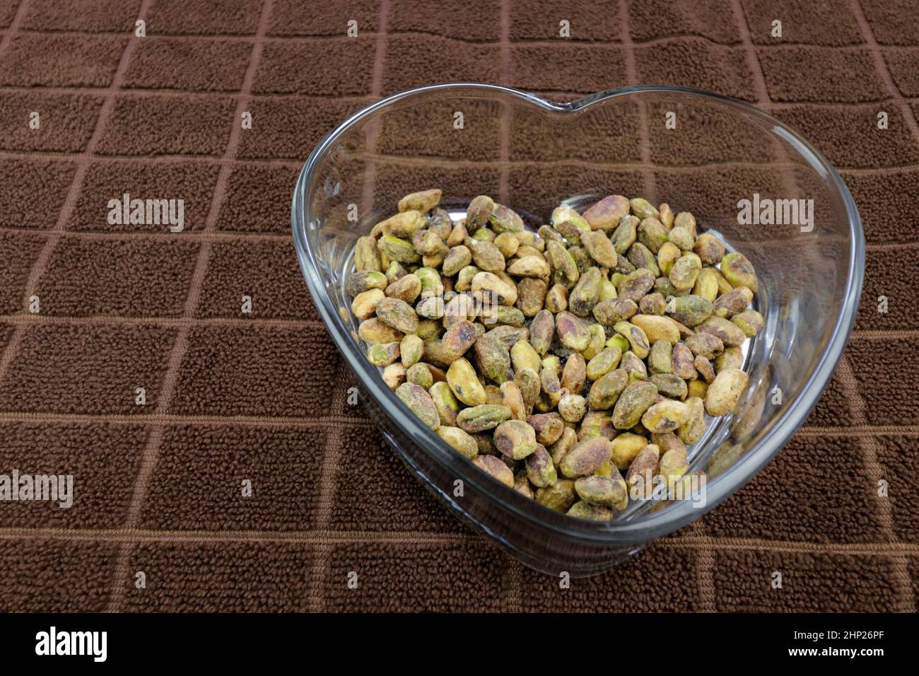 Roasted pistachios without shells with sea salt in a clear glass heart ...