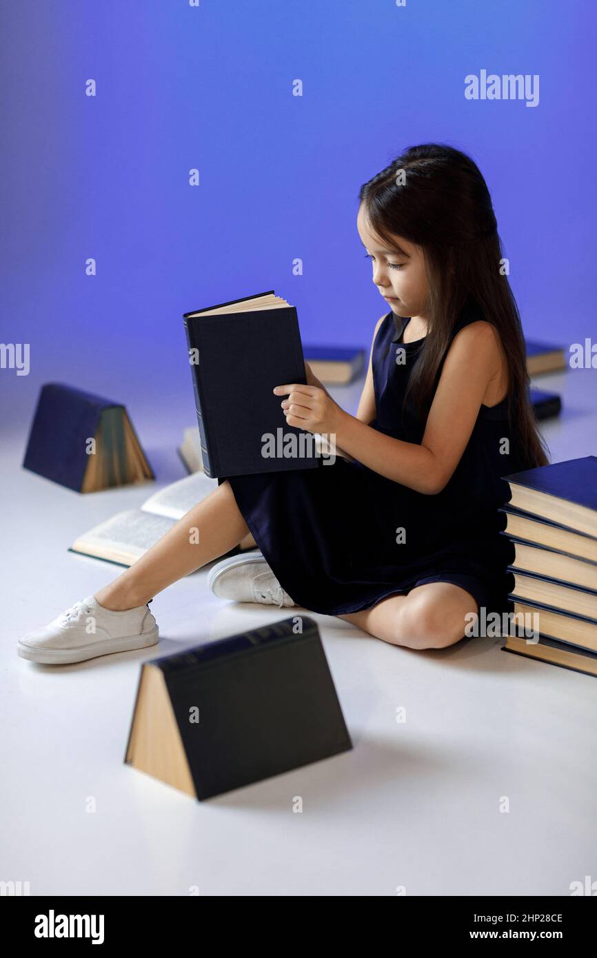cute little girl in dark blue dress is reading a book. child and a lot ...
