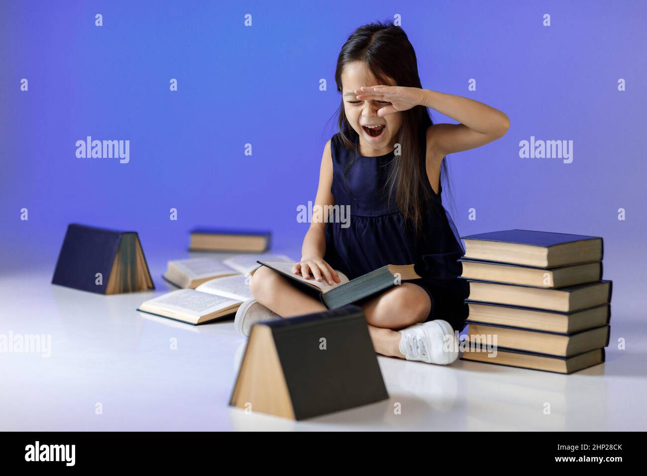 cute tired little girl in dark blue dress is reading a book. child and ...