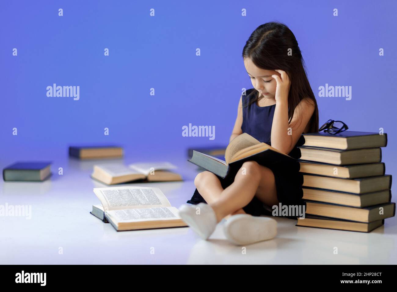cute little girl in dark blue dress is reading a book. child and a lot ...