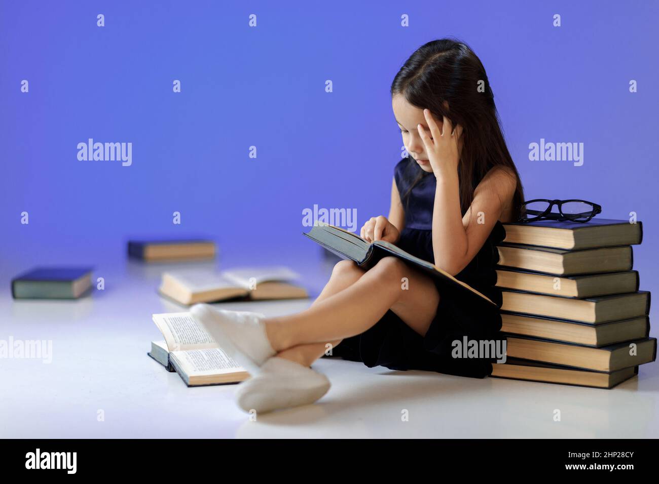 cute tired little girl in dark blue dress is reading a book. child and ...