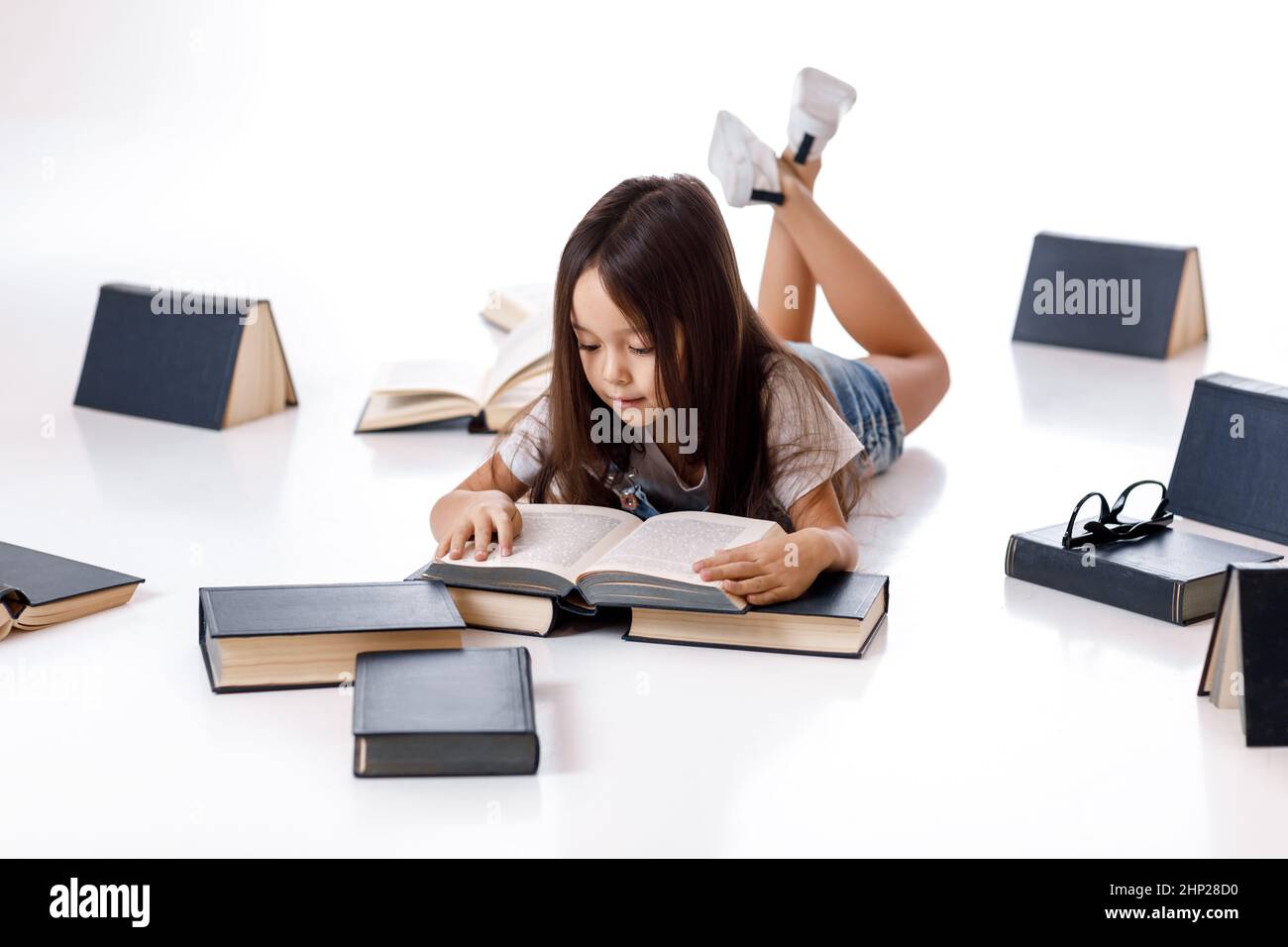 cute little child girl in denim is reading book on the floor with group ...