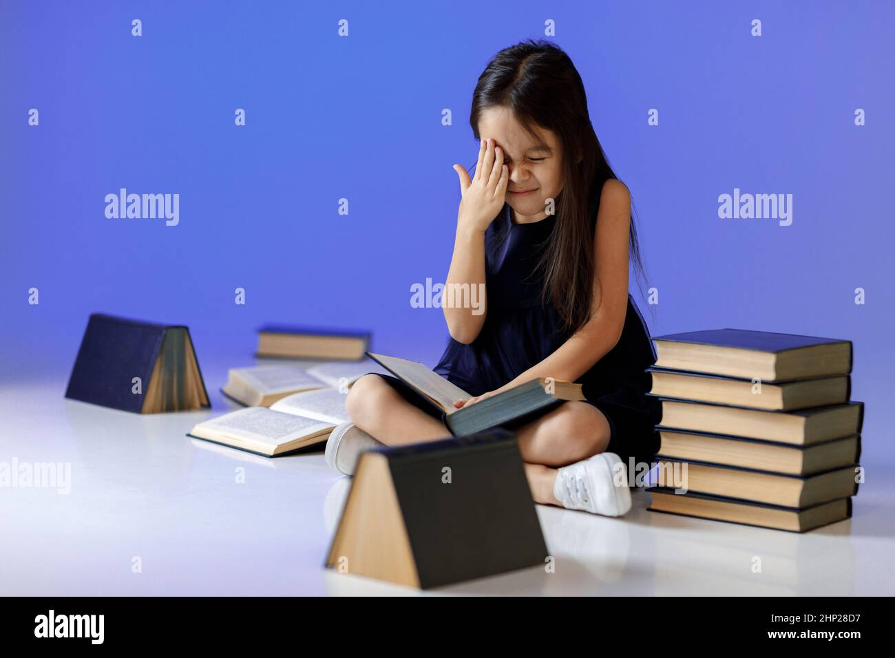 cute tired little girl in dark blue dress is reading a book. child and ...