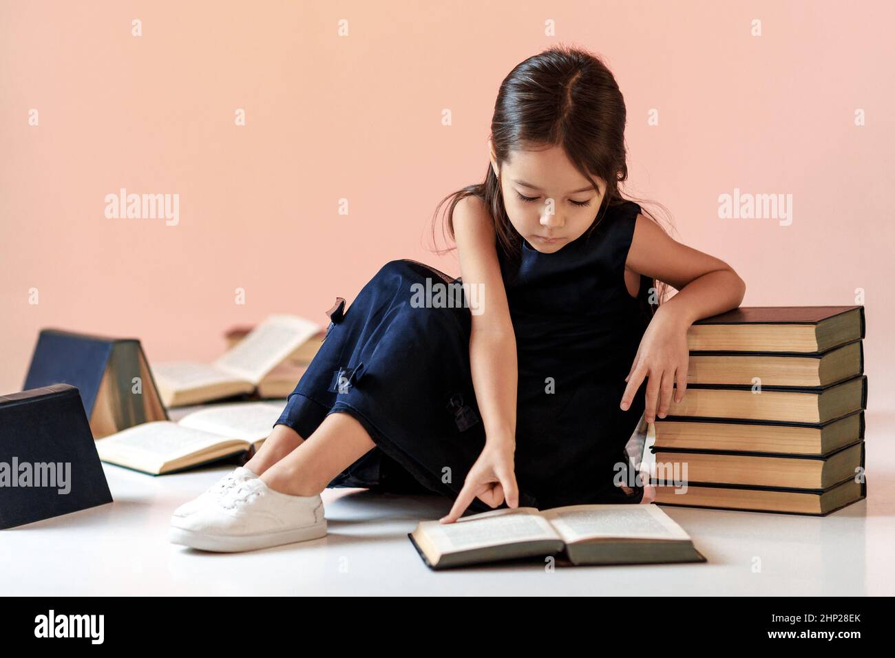cute little girl in dark blue dress is reading a book. child and a lot ...
