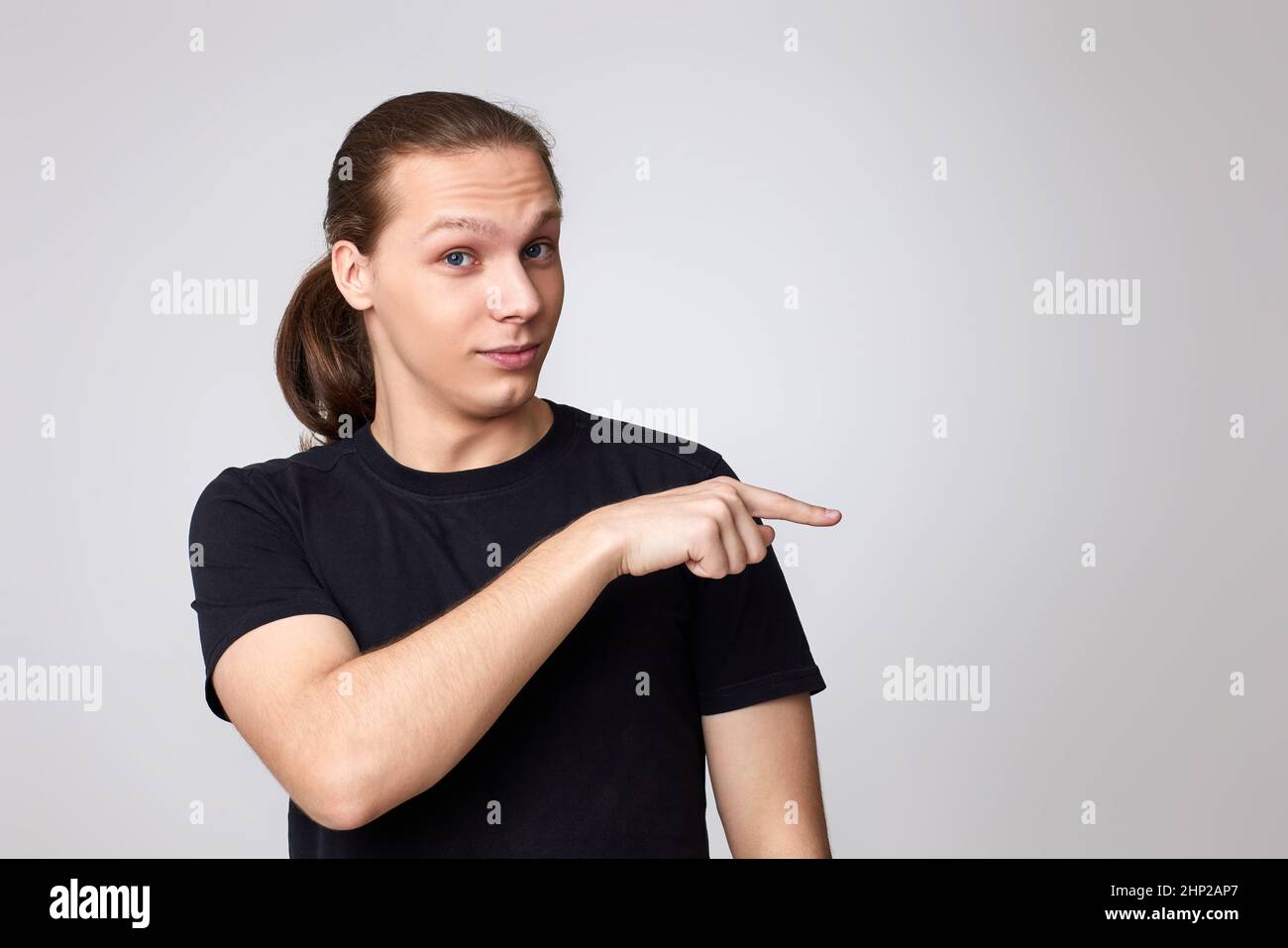 Positive young man pointing finger away at empty space for ...