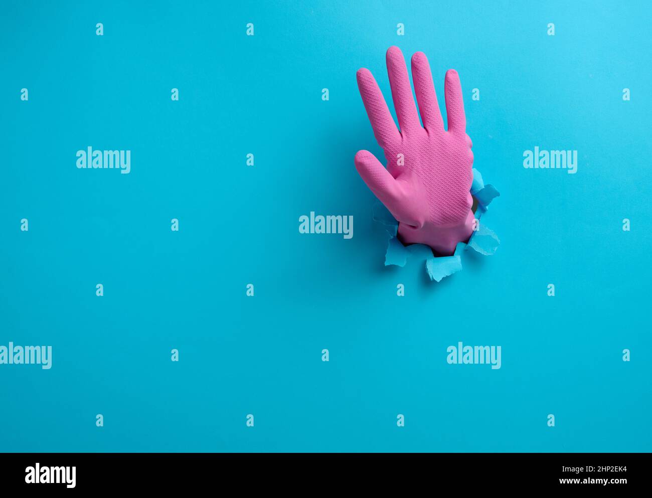 hand with an open palm sticks out of a torn hole in blue paper ...