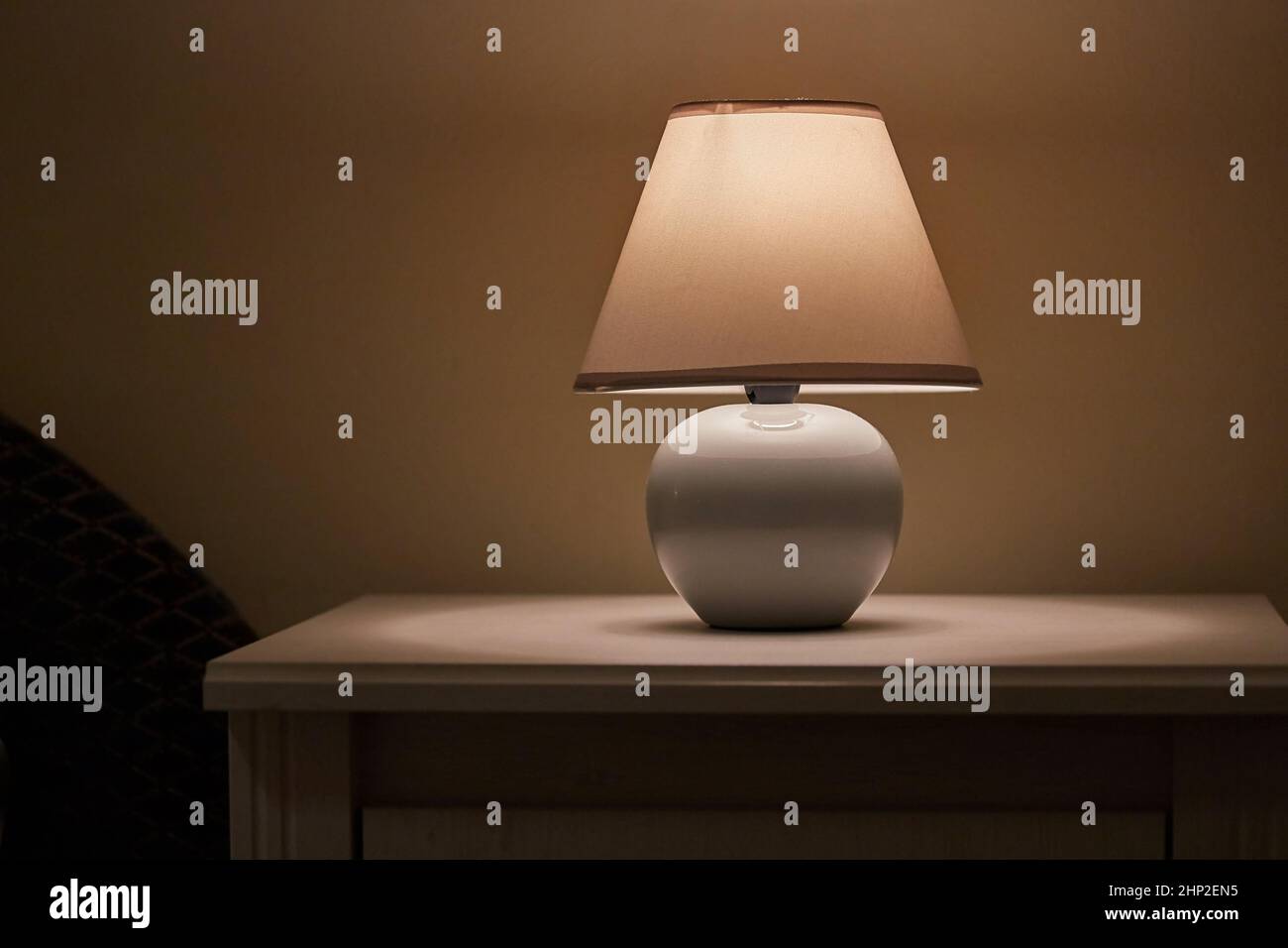 Small lamp glowing in bedroom night stand by the bedside, close up, dim ...