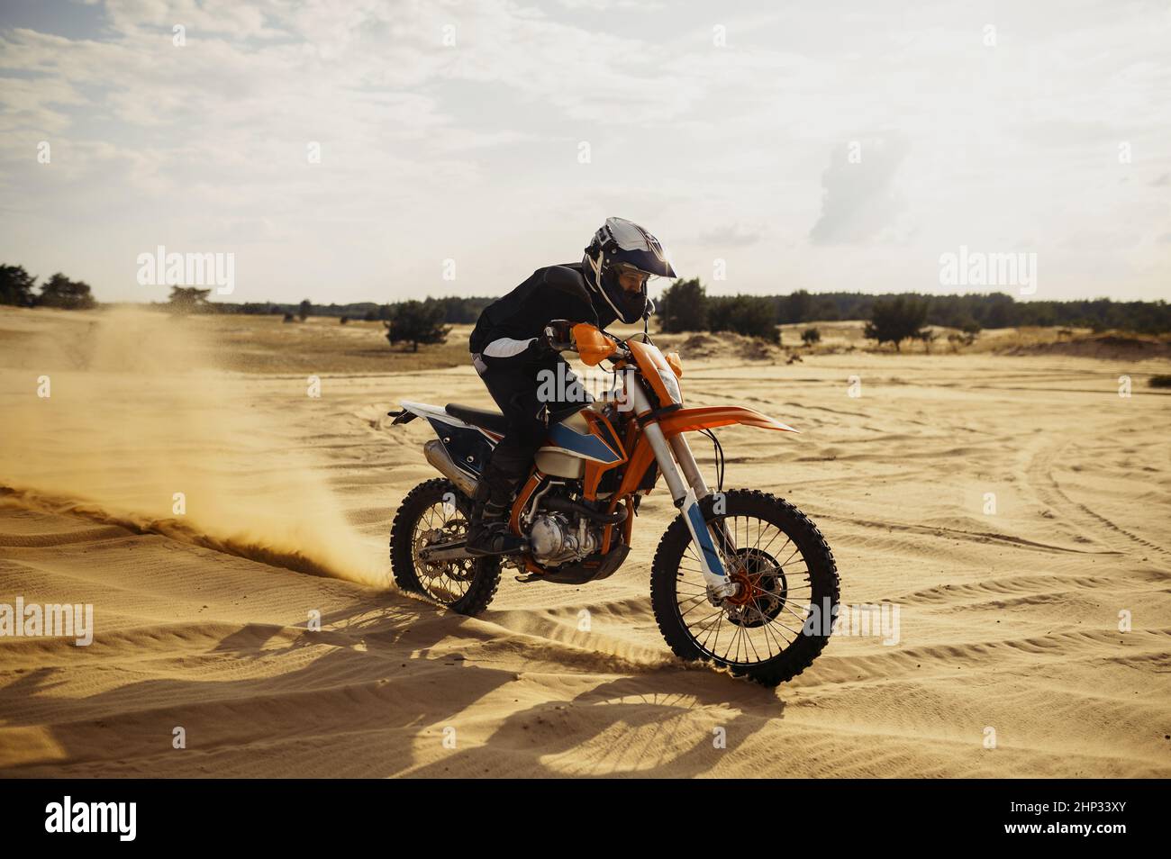 Motocross rider driving on sand dune further down off-road bike blowing ...