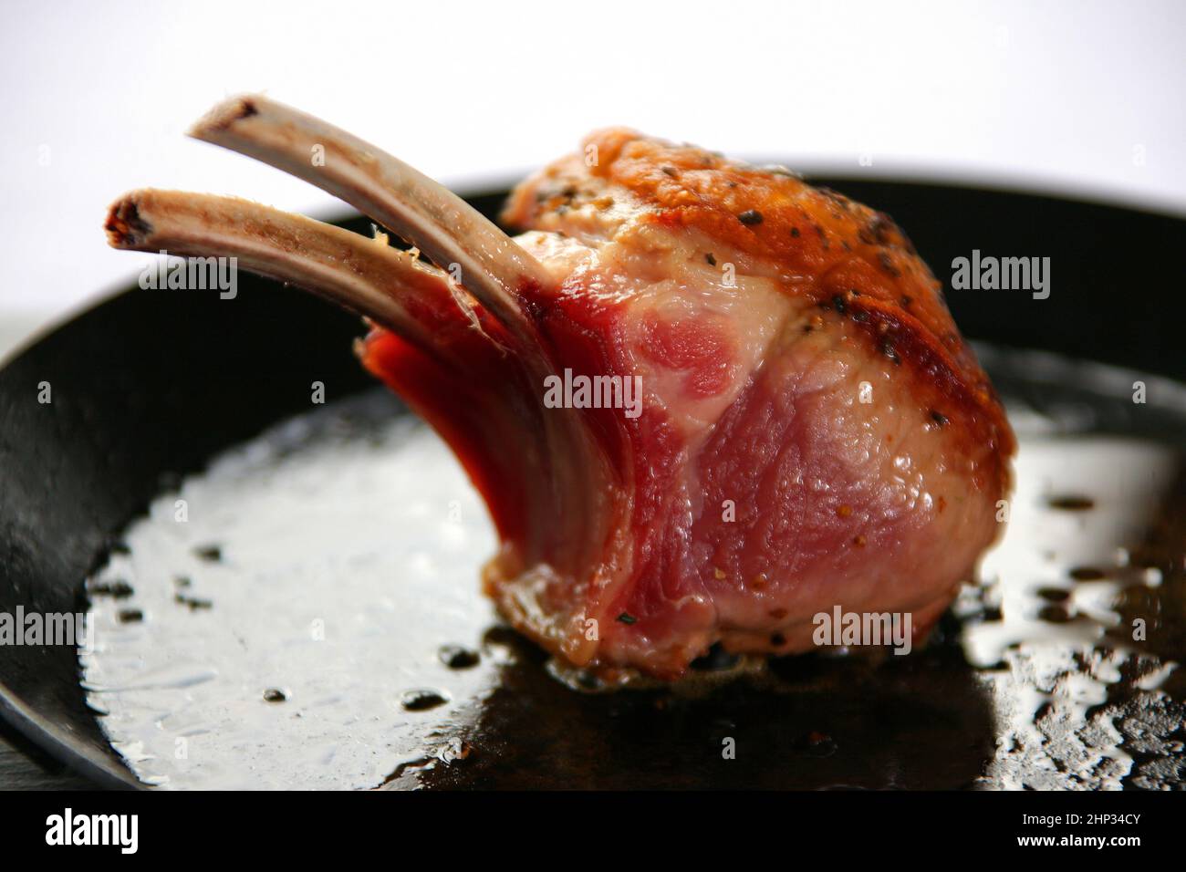 A rack of lamb searing in a black pan Stock Photo - Alamy