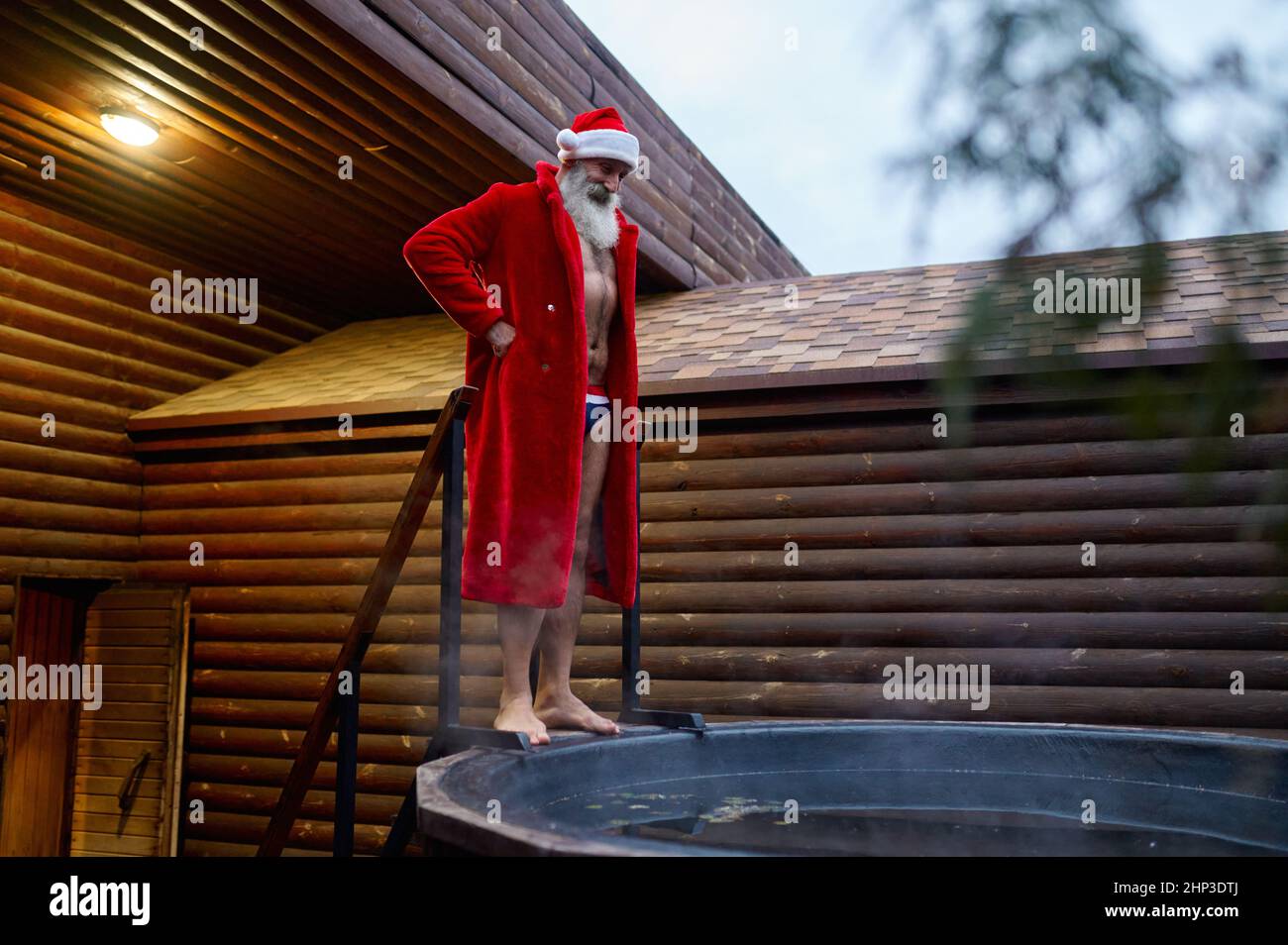 Santa Claus dressed in red bathrobe and hat standing at bathtub. Xmas ...