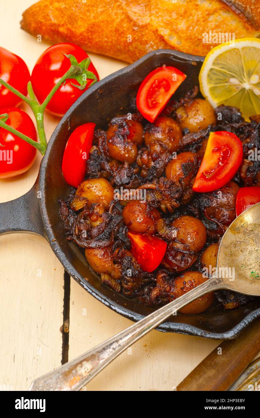Baby cuttle fish roasted on iron skillet with tomatoes and onions over ...