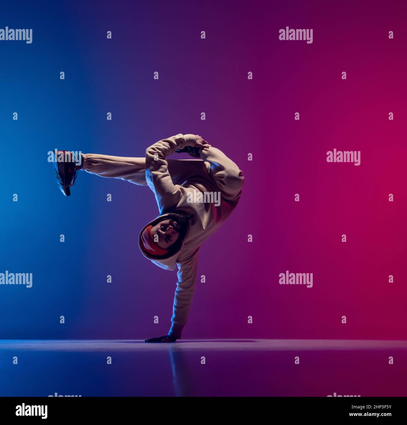 Studio shot of young flexible sportive man dancing breakdance in white outfit on gradient pink ...