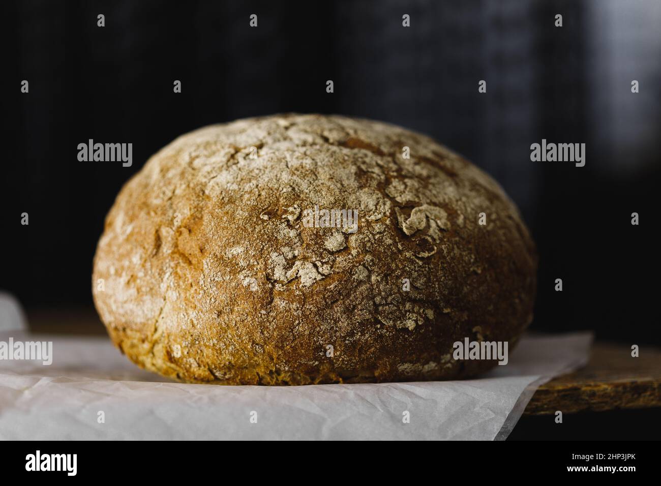 round bread with a bright crispy crust lies on parchment on a wooden ...
