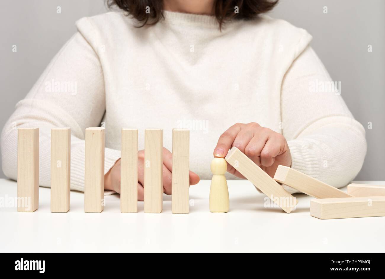 hand stops the fall of wooden figurines of men on a white background ...