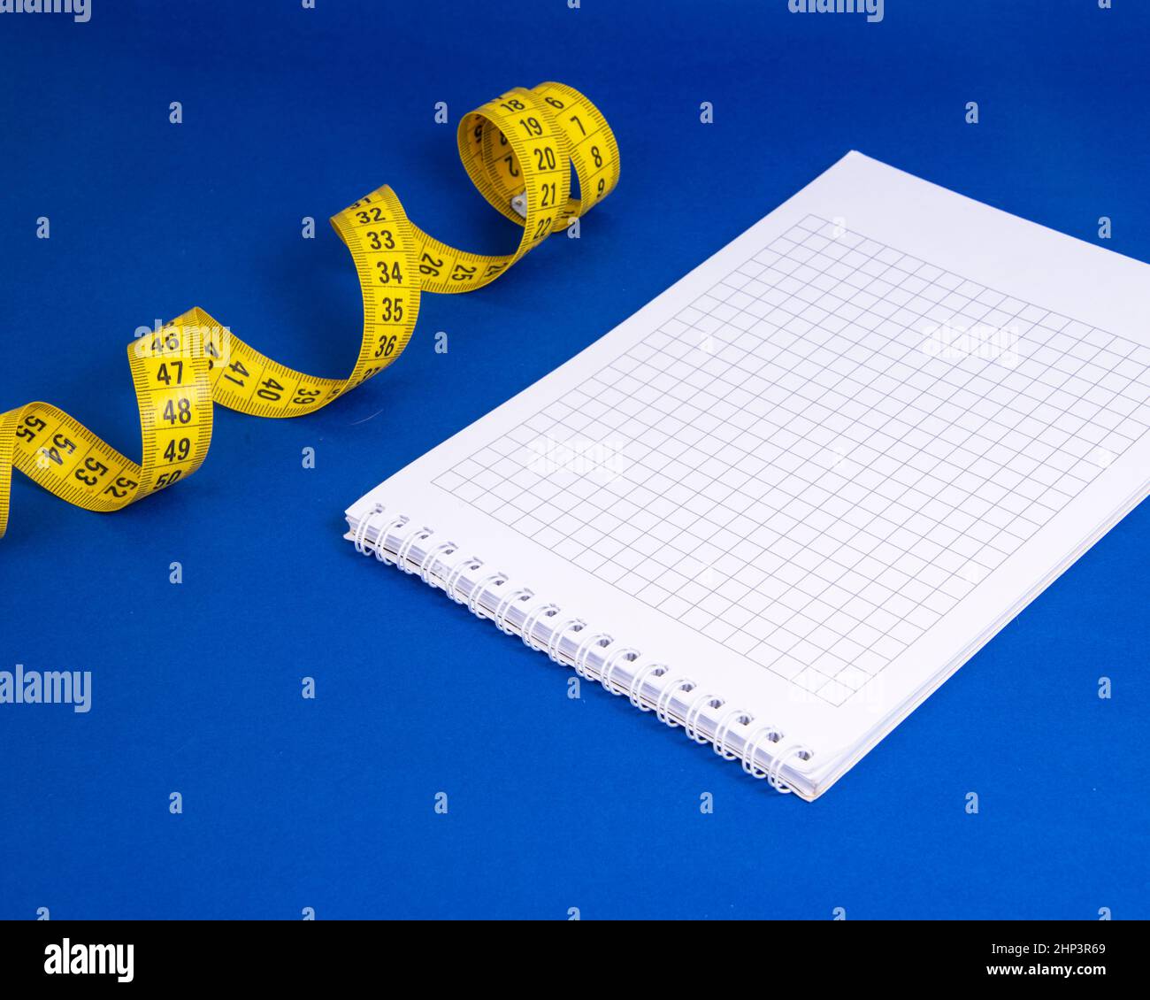 Yellow spiral tape measure and notebook on dark blue background Stock ...