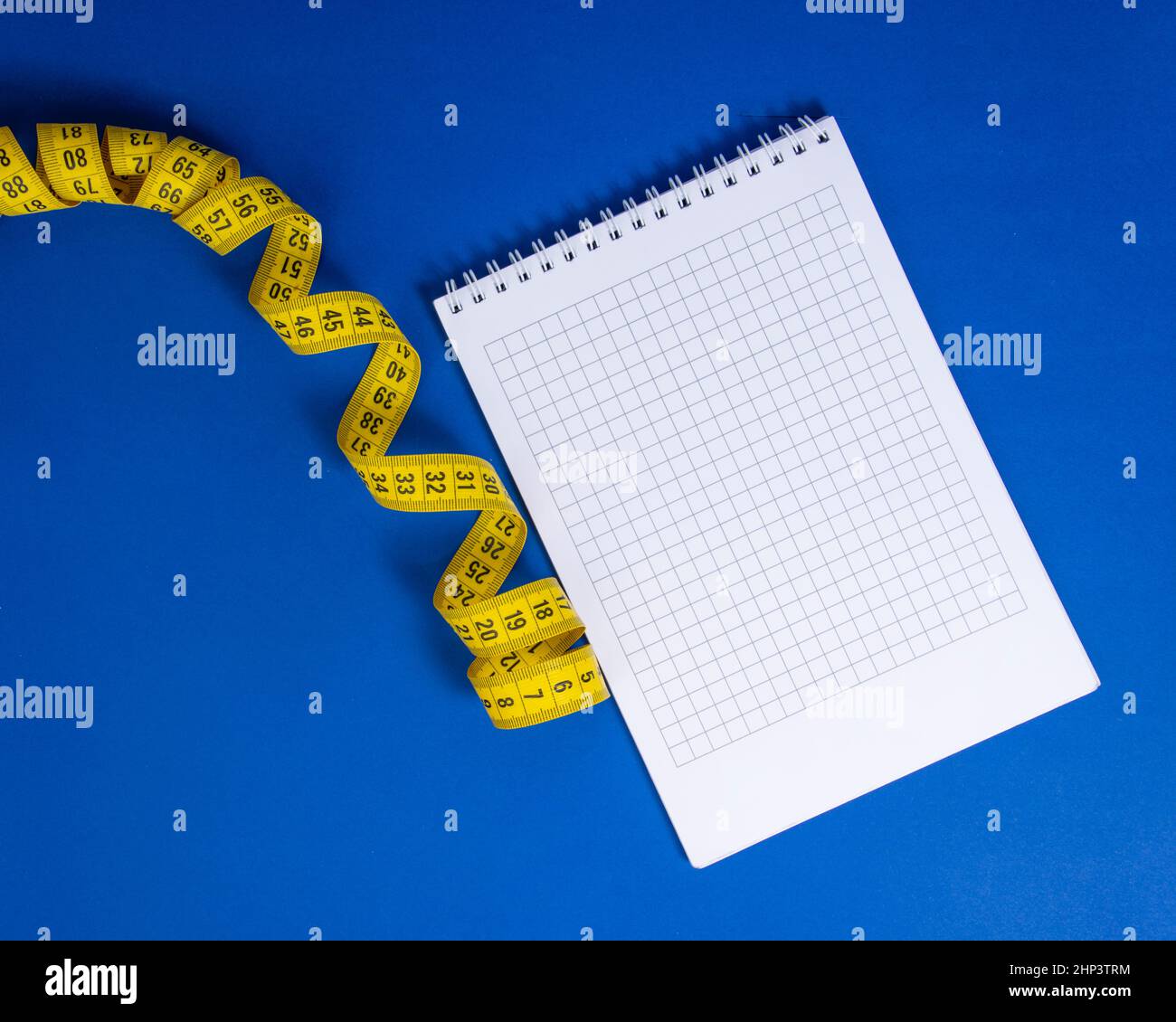 Yellow spiral tape measure and notebook on dark blue background Stock ...