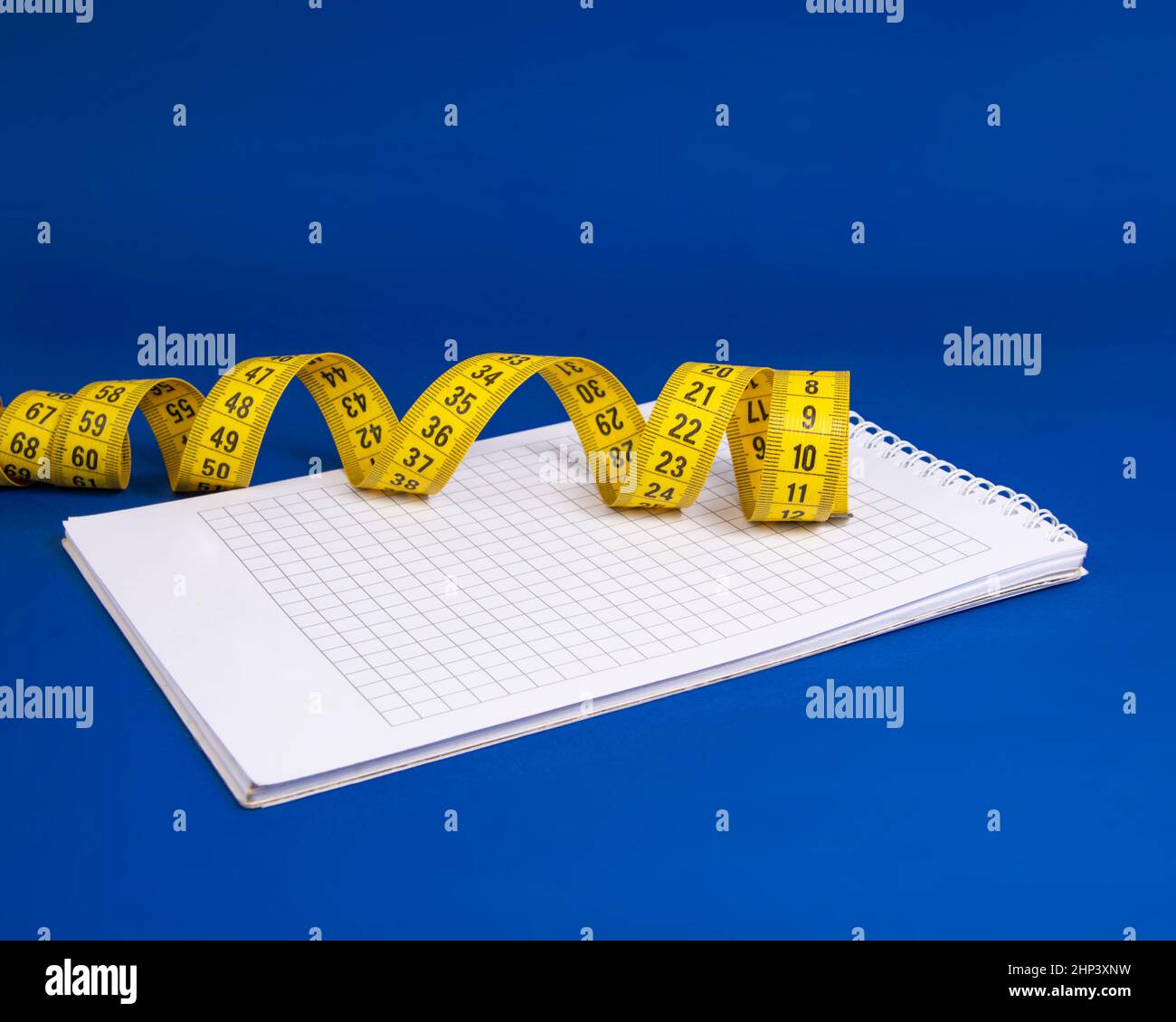 Yellow spiral tape measure and notebook on dark blue background Stock ...