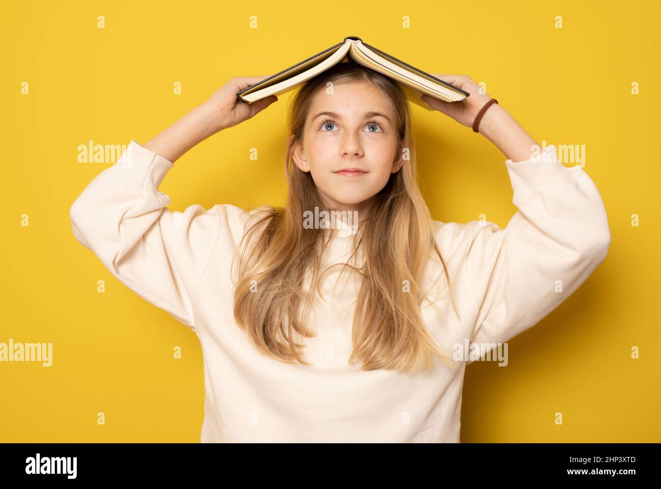 Beautiful girl with a book on her head isolated over yellow background ...