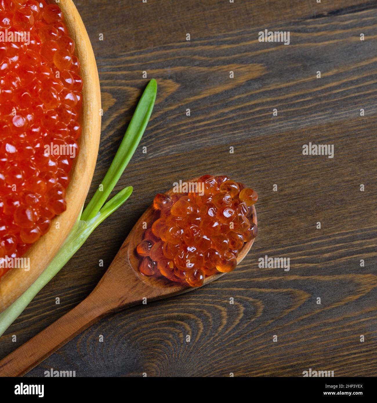 Red caviar in a wooden cup on a wooden background with a spoon. Place ...