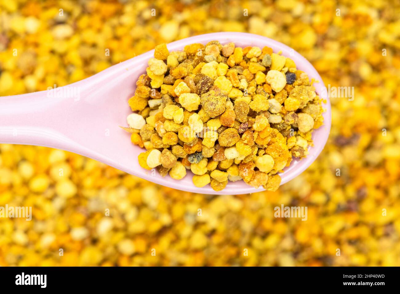 top view of pink ceramic spoon with natural bee pollen close up over blurred bee bread on ...