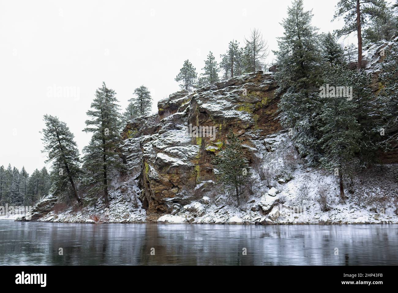 Snow covered outcropping of the hill next to the calm Spokane river ...