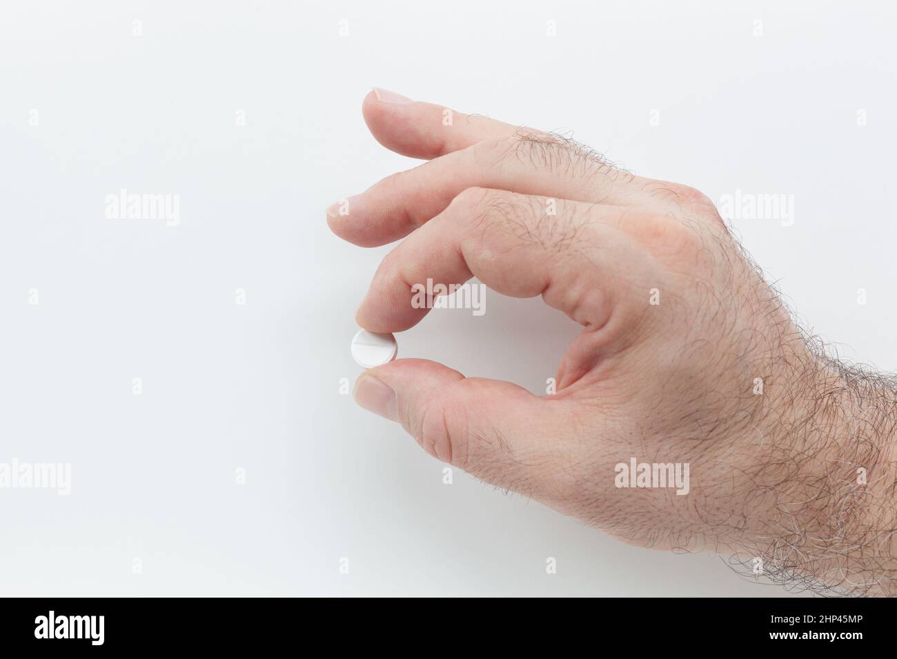 Male hand holding white medicine pill between thumb and index finger ...