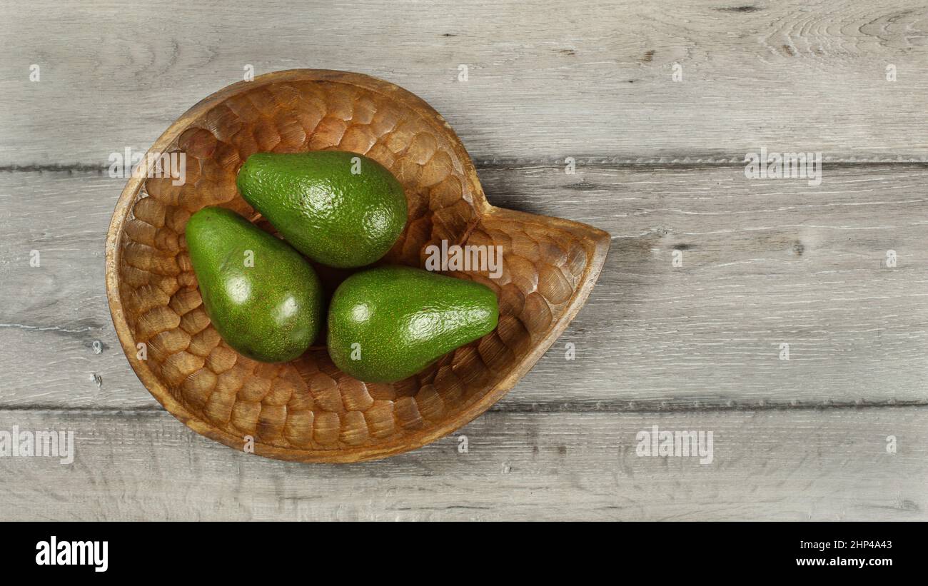 Tabletop view, three avocado pears on wooden carved bowl Stock Photo ...