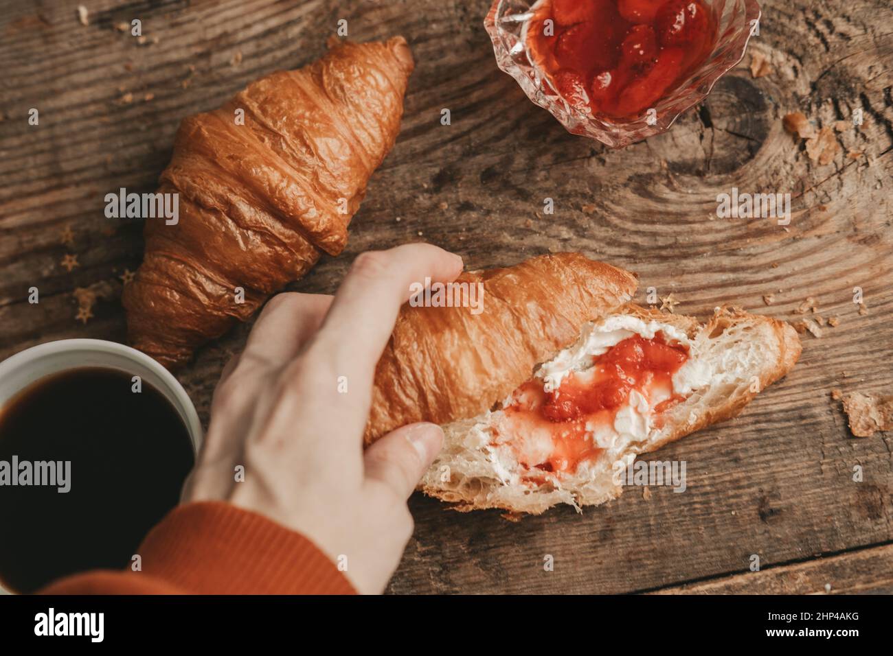 hand holding cut croissant with butter and strawberry jam on wooden ...