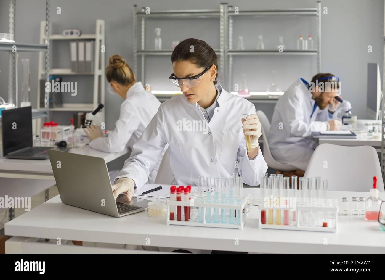 Female scientist in lab or chemist making notes on laptop by studying ...