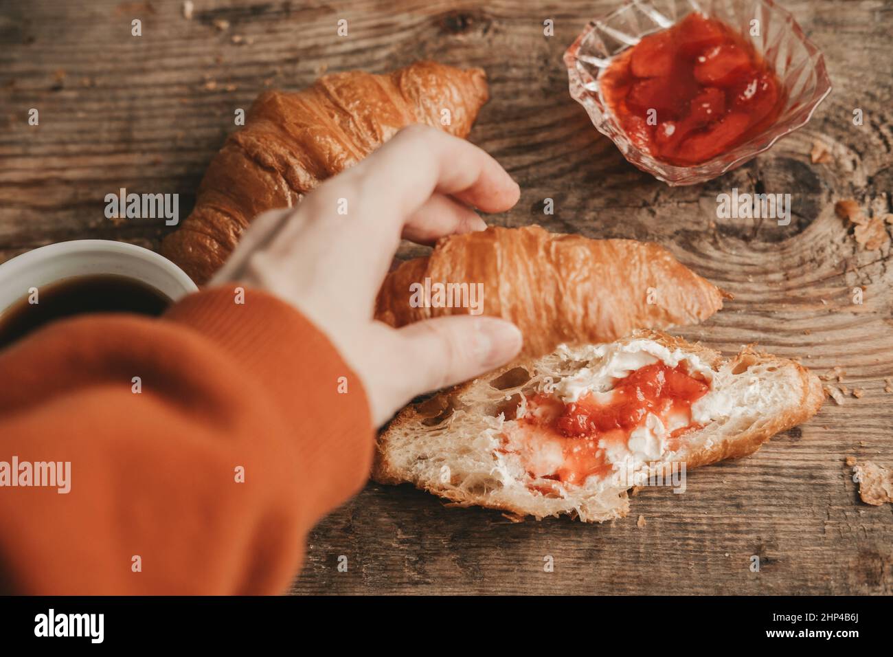 hand holding cut croissant with butter and strawberry jam on wooden ...