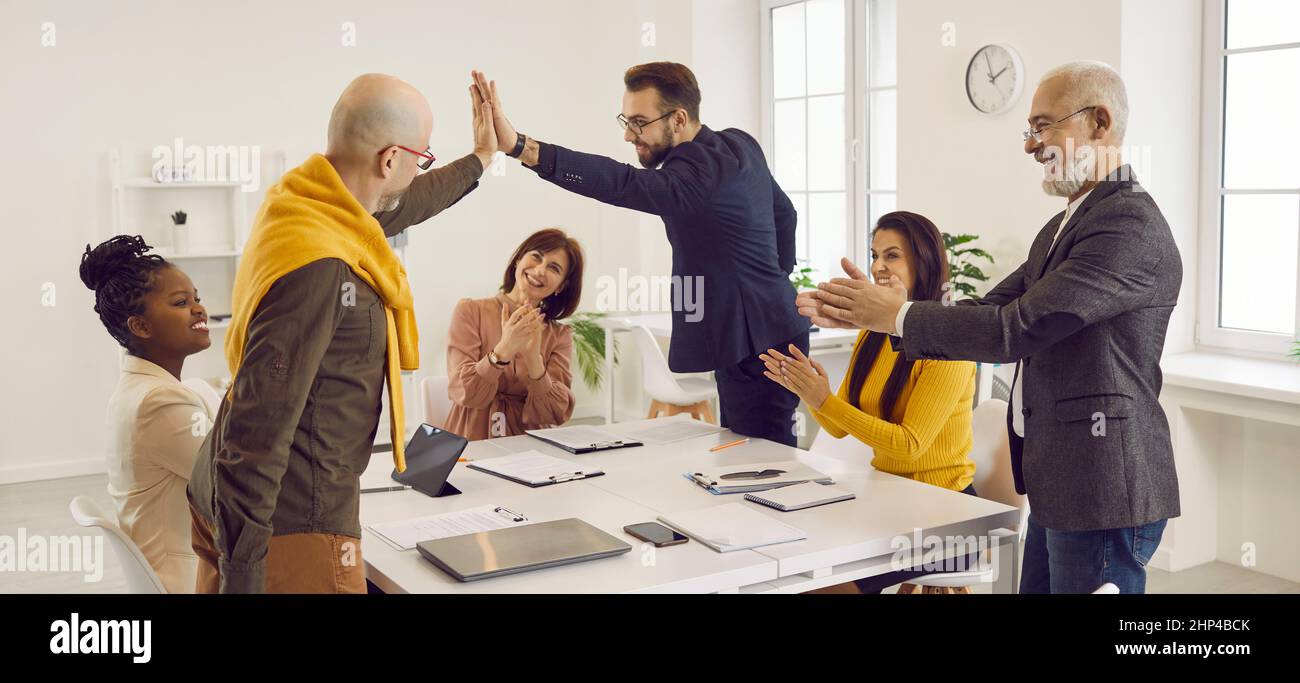 Happy men give each other high five as they celebrate success during ...
