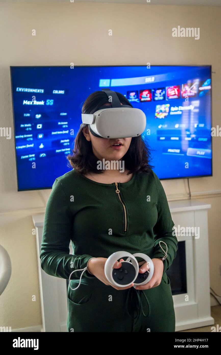 Girl with VR headset and two controllers playing with friends in ...