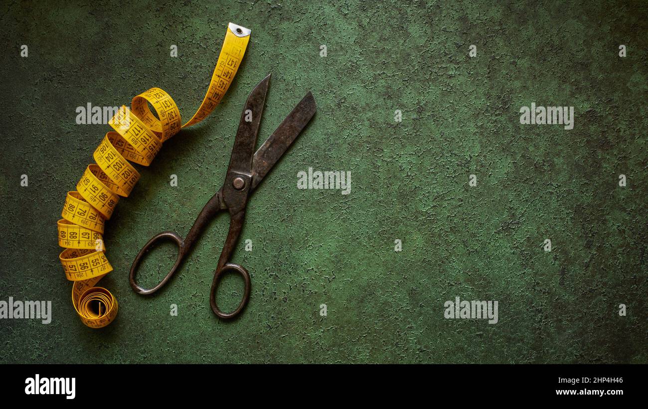 Antique tailor scissors and a tape measure on dark green textured ...