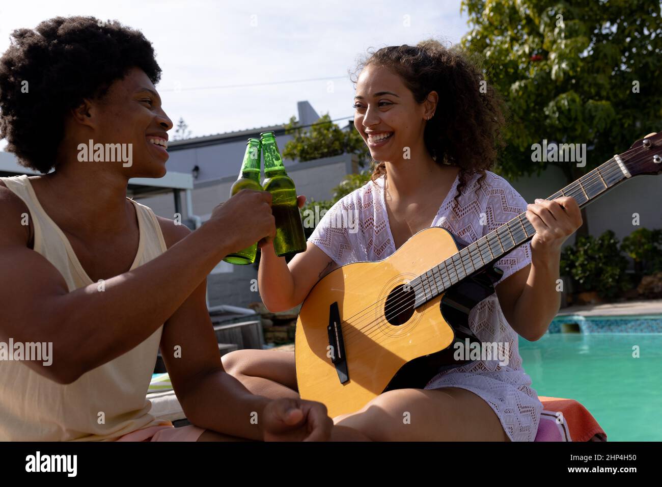 Happy biracial woman with guitar toasting beer bottle with man at ...