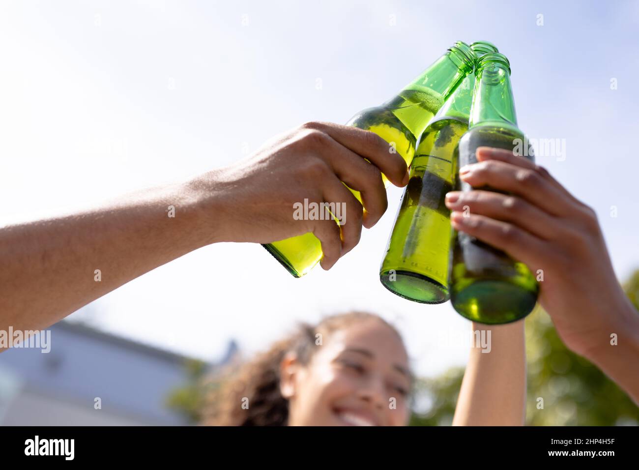 Low angle view of biracial women and men's hands toasting beer bottles ...