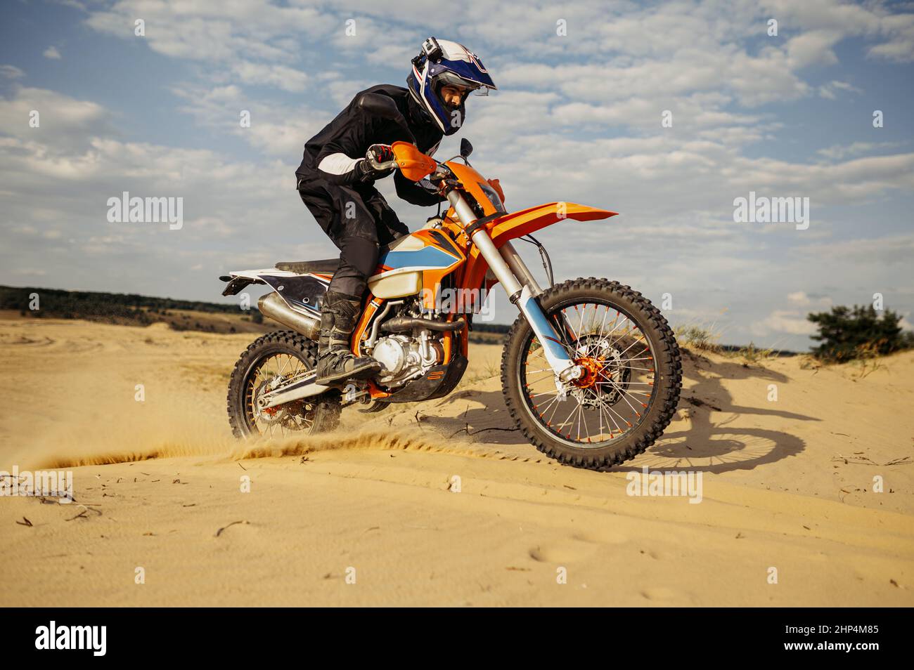 Motocross rider driving on sand dune further down off-road bike blowing ...