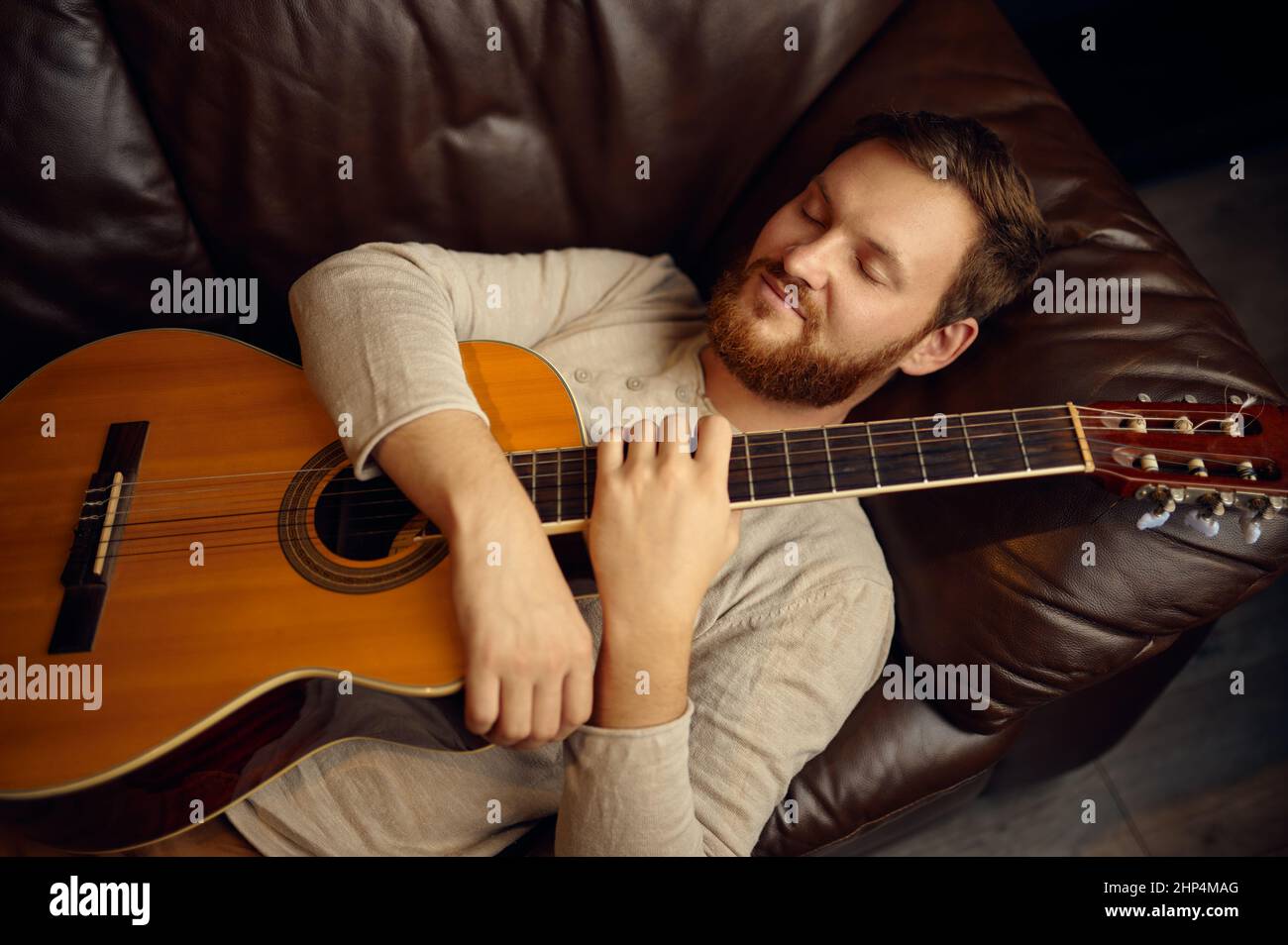Young man lying on sofa hugging guitar. Guitarist player passion and ...