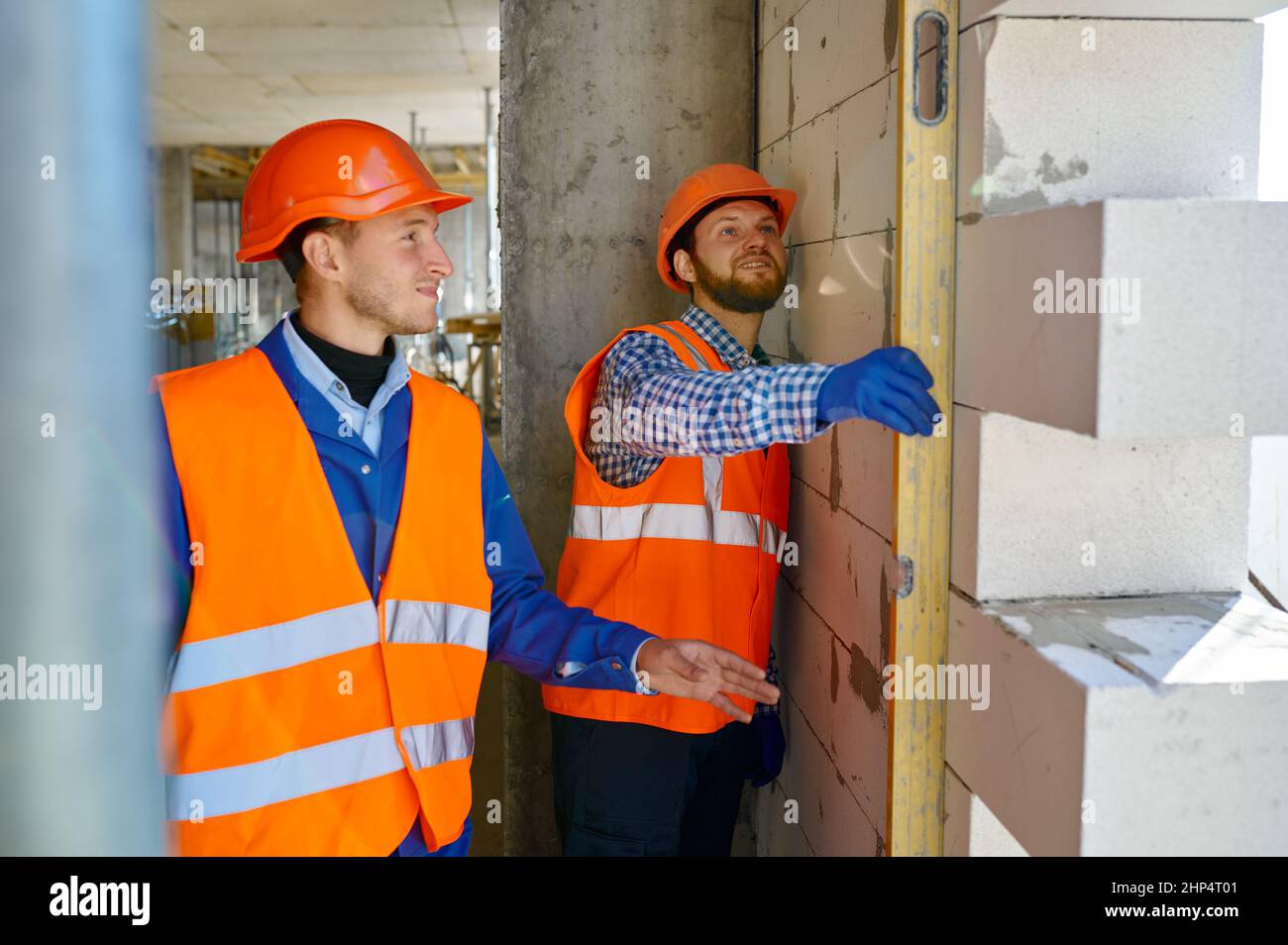 Two bricklayer builders checking wall level with special tool. High ...