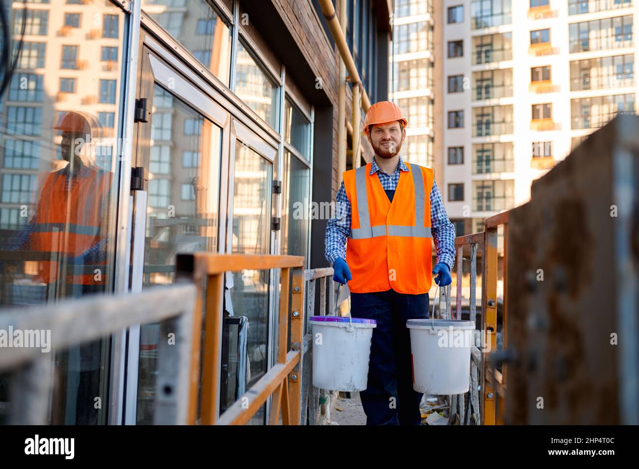Male construction worker carrying buckets of cement, plaster or paint ...