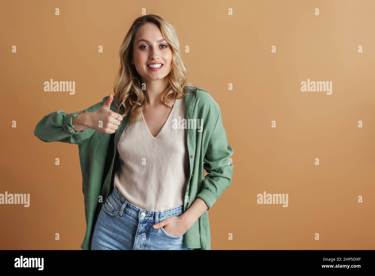 Happy beautiful woman smiling and showing thumb up isolated over beige ...