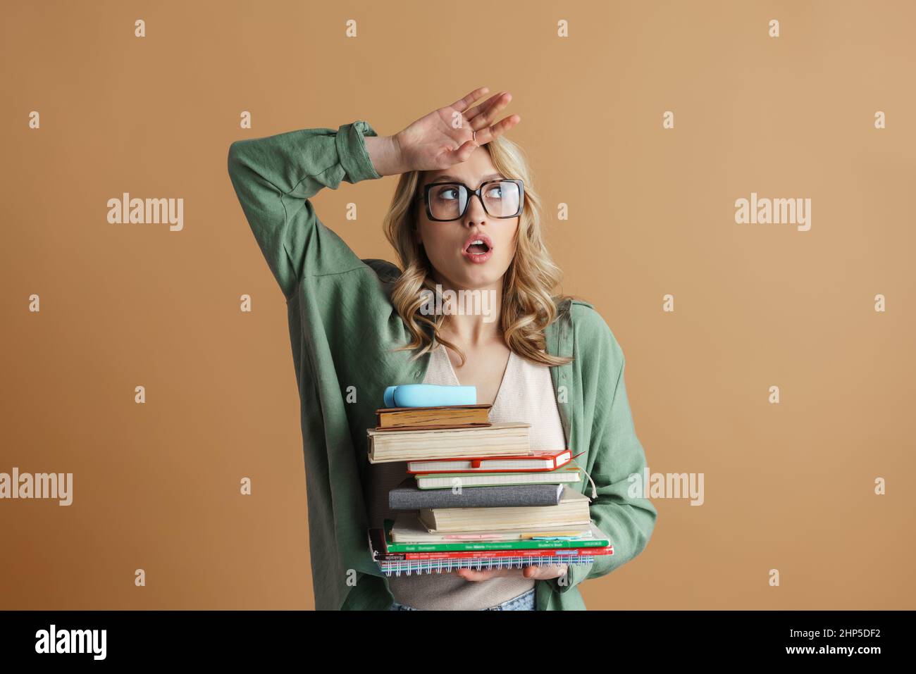 Exhausted beautiful woman in eyeglasses posing with books and planners ...