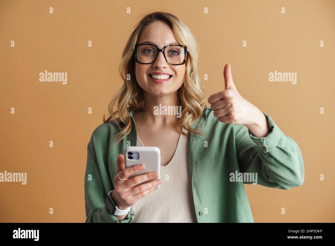 Happy woman showing thumb up while using mobile phone isolated over ...
