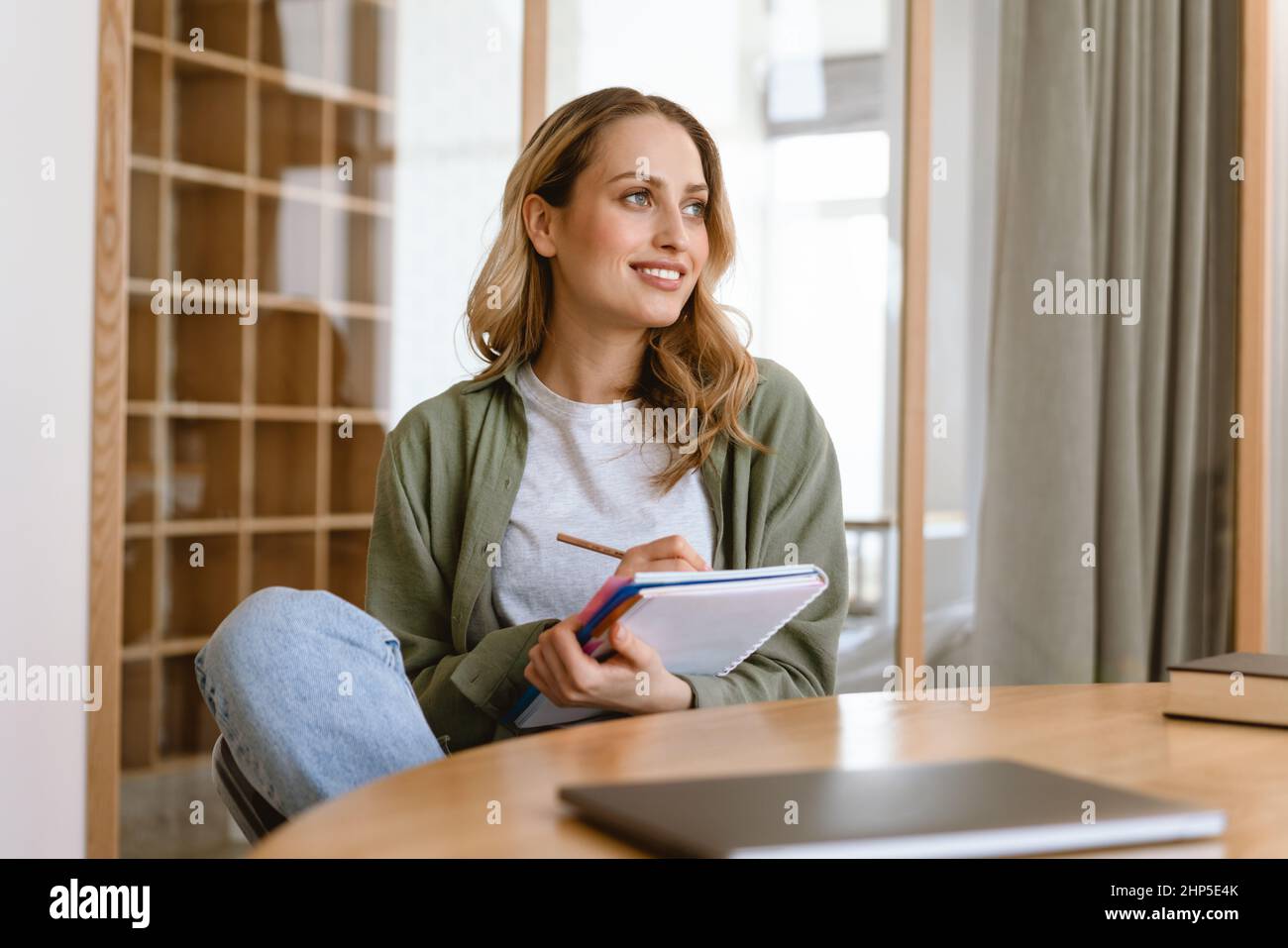 Smiling young white blond woman writing down notes while sitting at ...